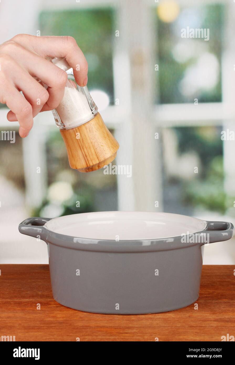 Hand adding salt using salt shaker on bright background Stock Photo - Alamy