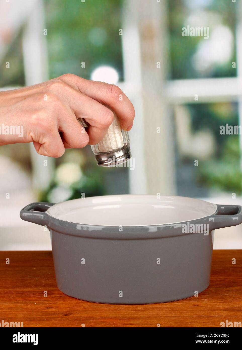 Hand adding salt using salt shaker on bright background Stock Photo - Alamy