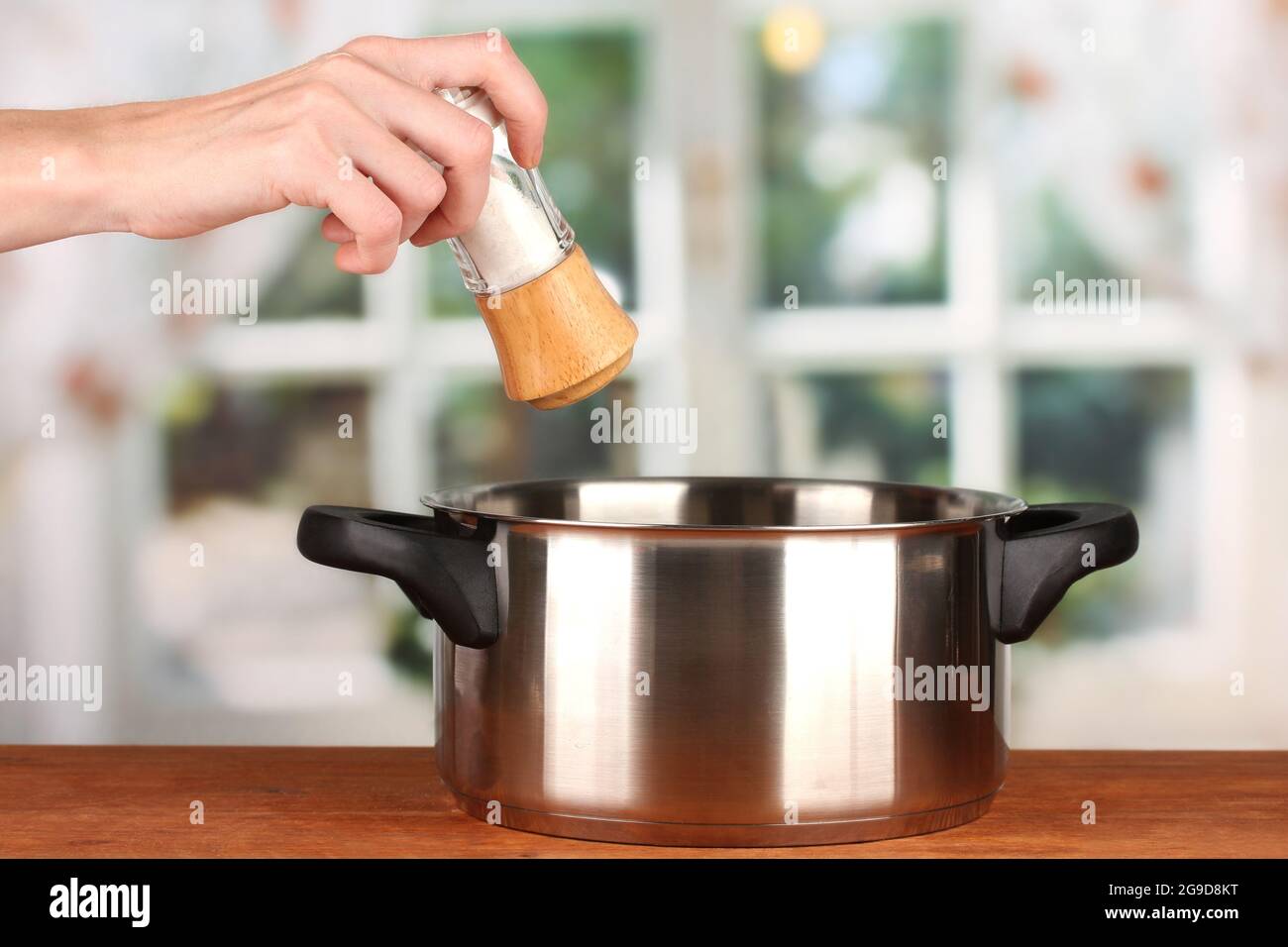 Hand adding salt using salt shaker on bright background Stock Photo - Alamy