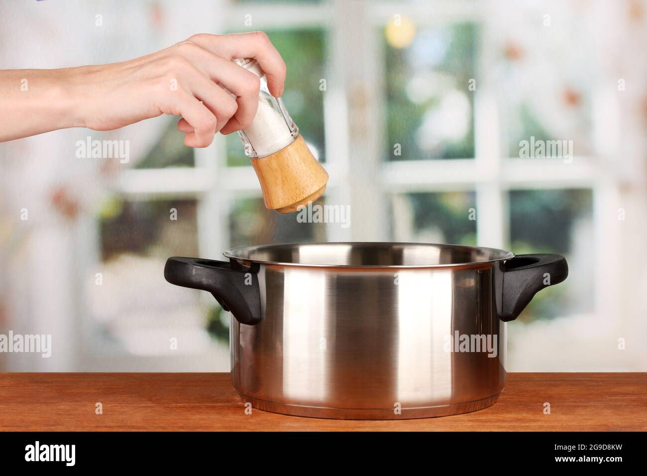 Hand adding salt using salt shaker on bright background Stock Photo - Alamy