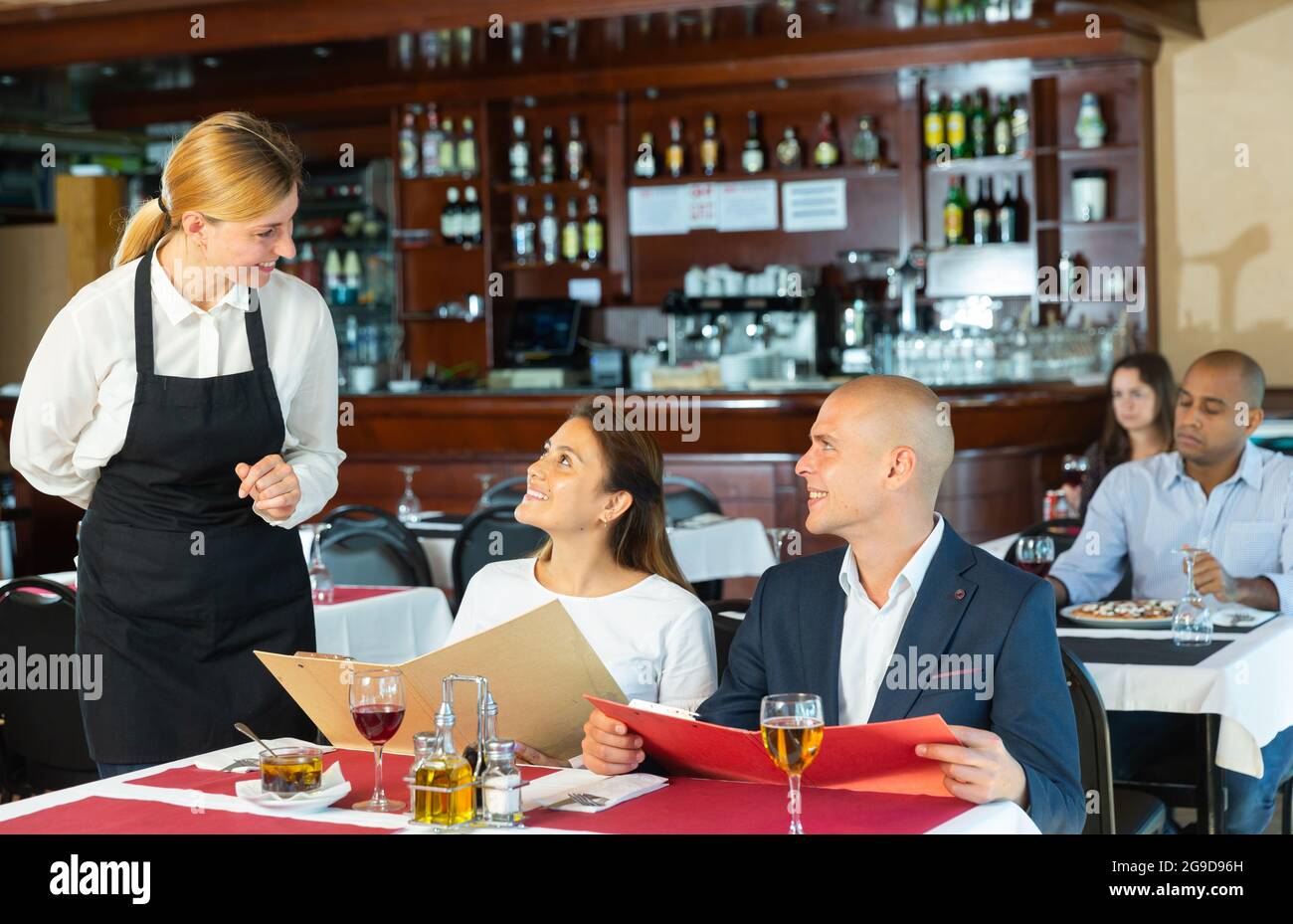 Diligent friendly smiling pleasant waitress taking order from couple ...