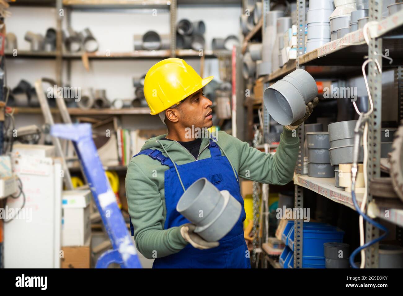 Worker in overalls lays out plumbing fittings on the shelves of ...