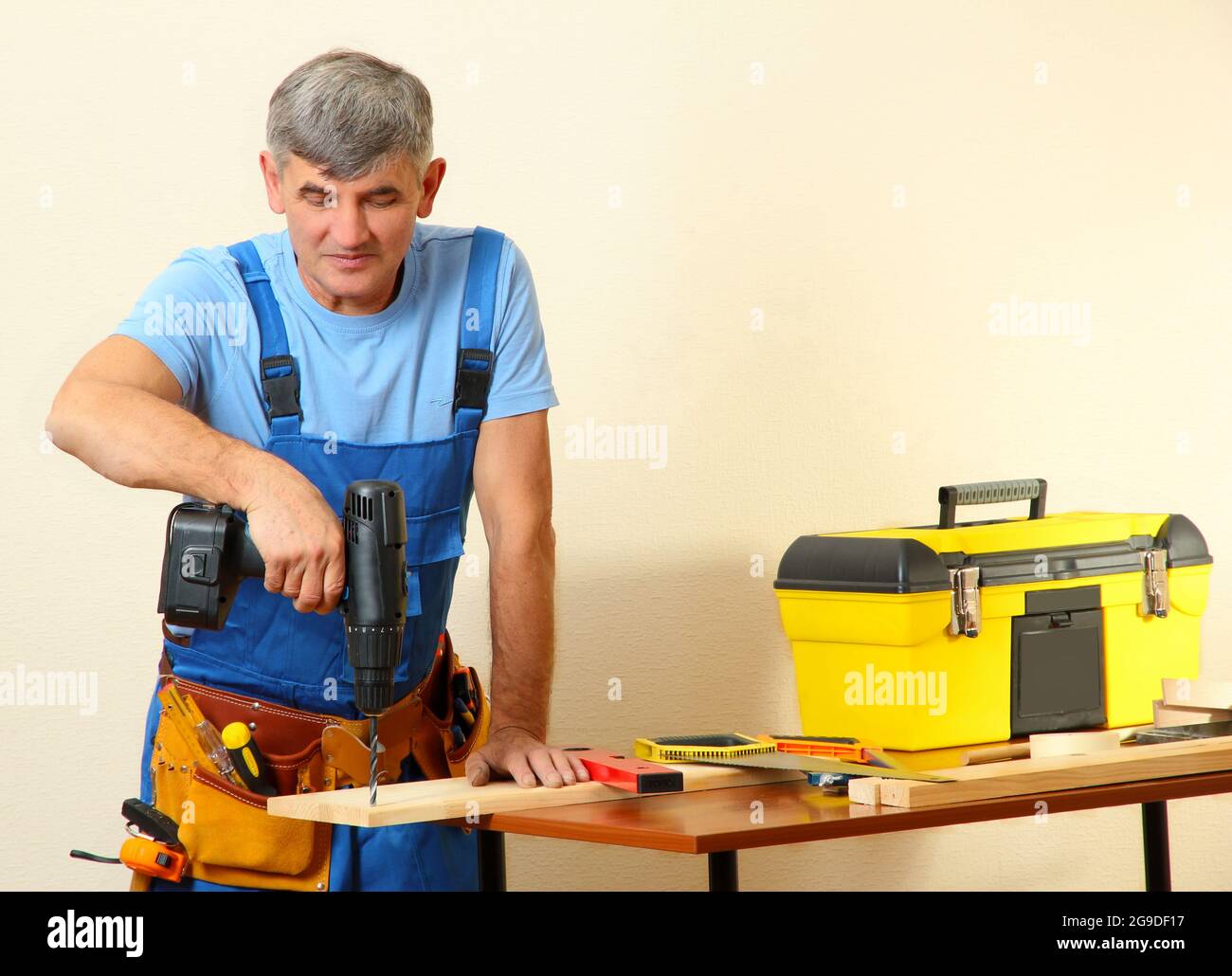 Builder drills board on table on wall background Stock Photo - Alamy