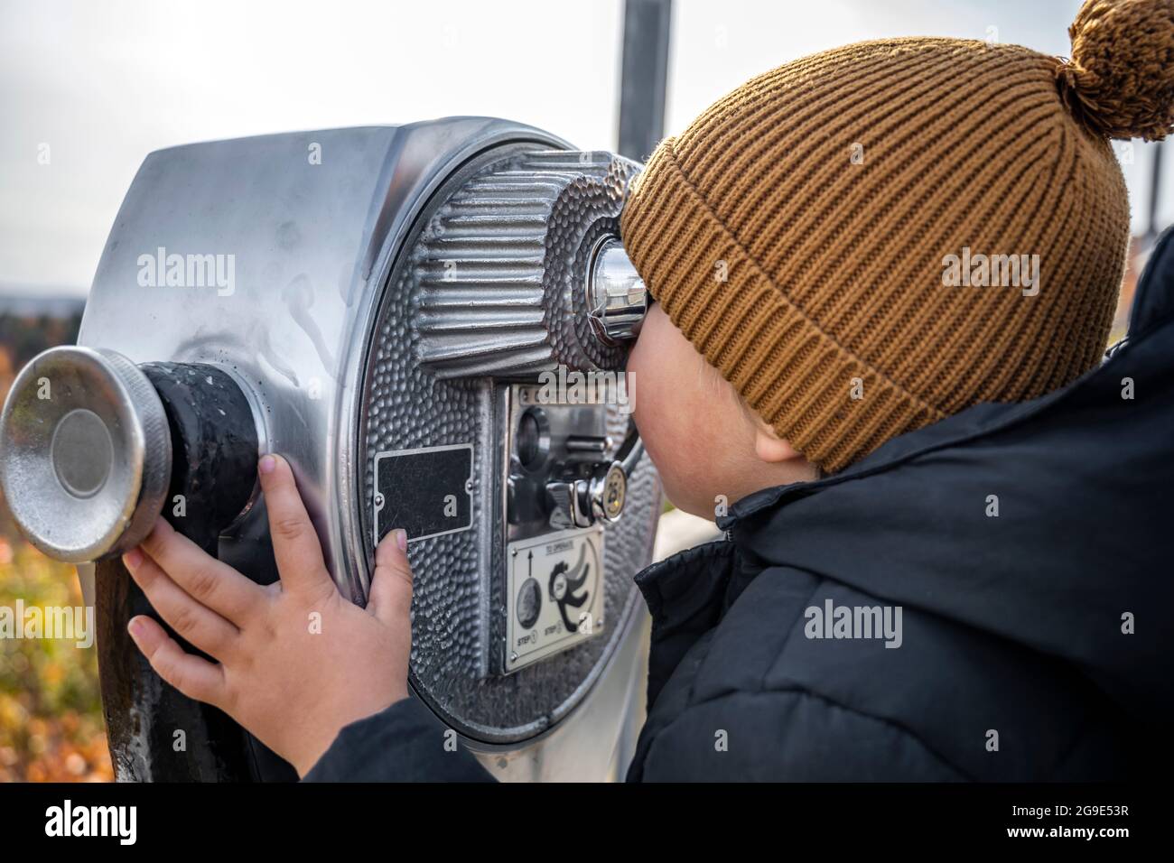 A little boy in a brown knitted woolen hat looks through the stationary ...