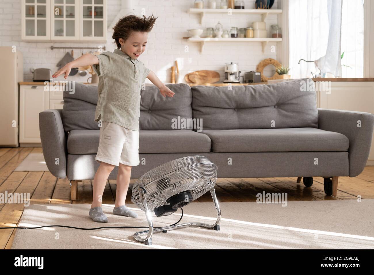 Little boy enjoy air flow from fan in living room. Cute small kid play ...