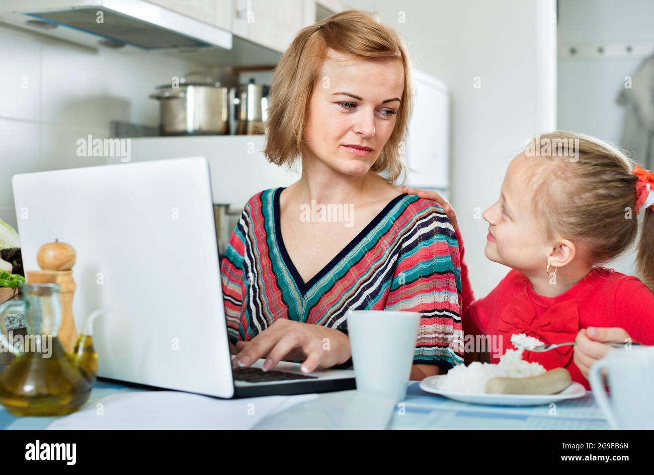 Smiling woman sitting in the kitchen with daughter Stock Photo - Alamy