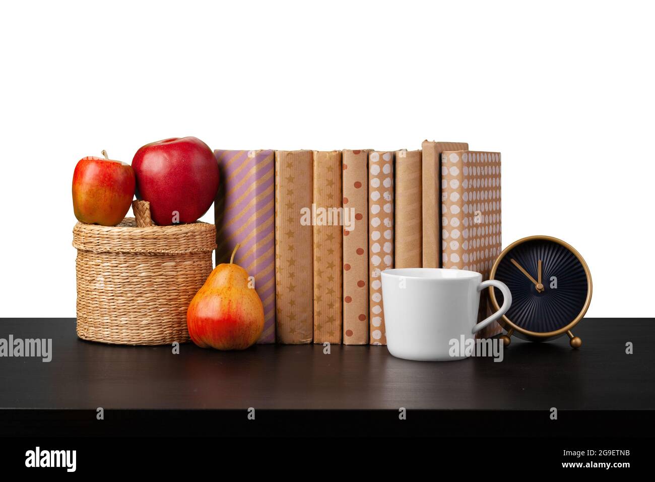 Alarm clock, stack of books and cup on tabletop against white ...
