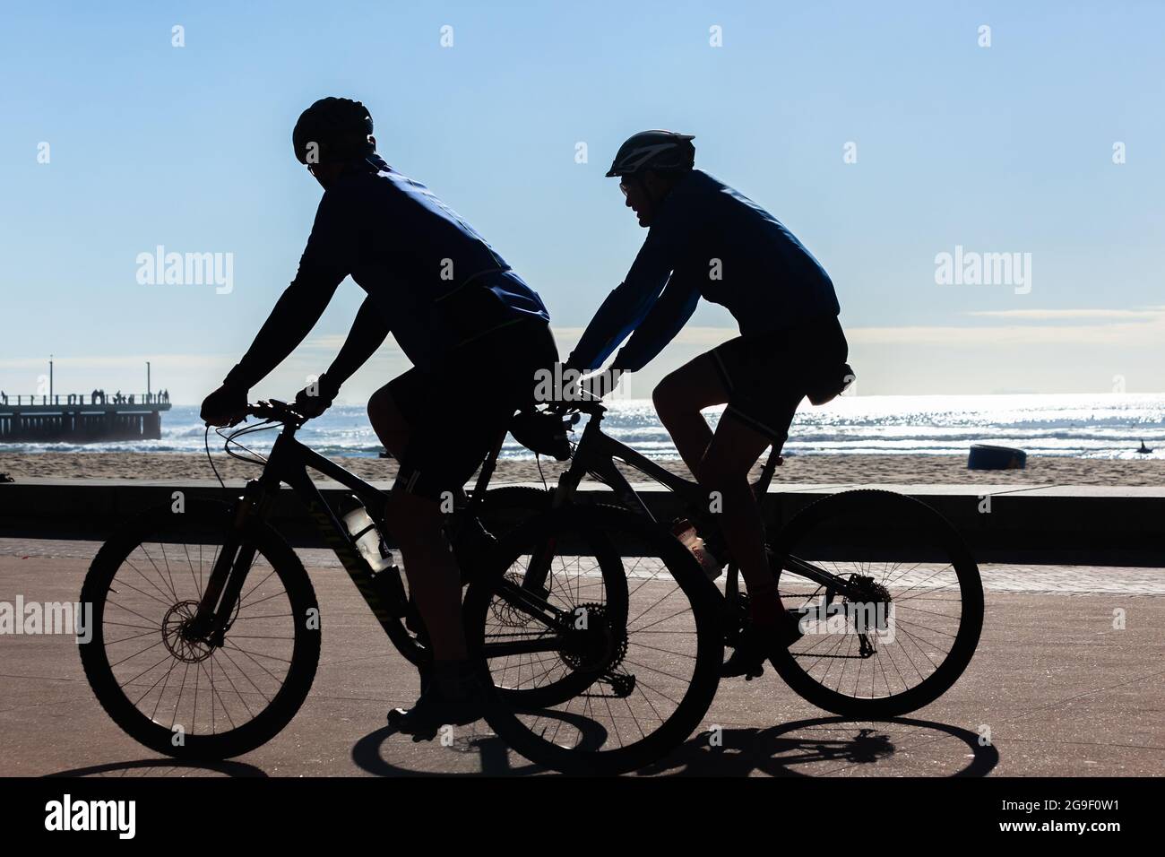 Cycling two riders on bicycles silhouetted unrecognizable riding beach ...