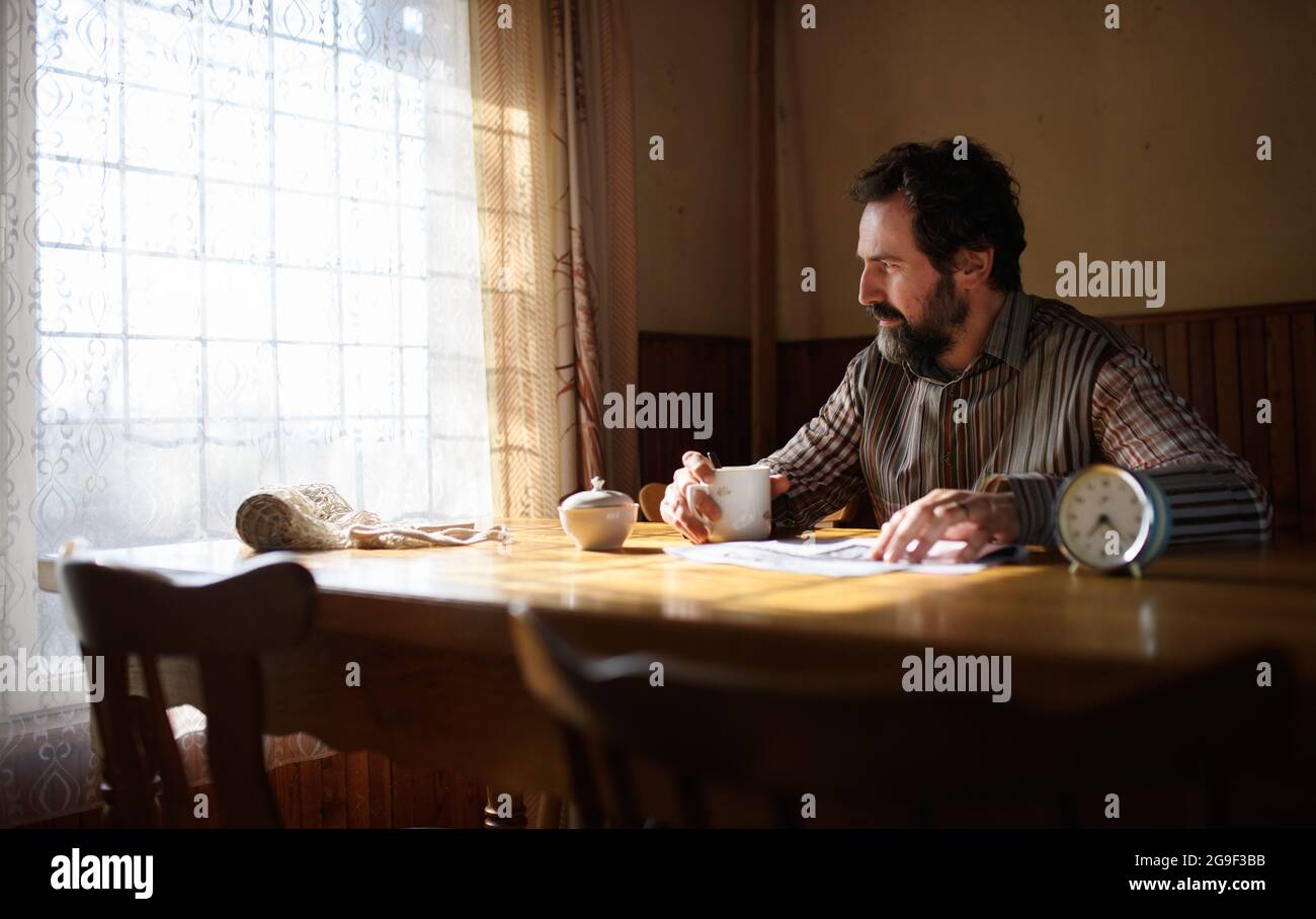 Portrait of unhappy poor mature man reading newspapers indoors at home ...