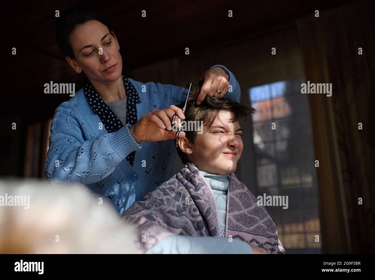 Portrait of poor woman cutting daughter's hair indoors at home, poverty ...