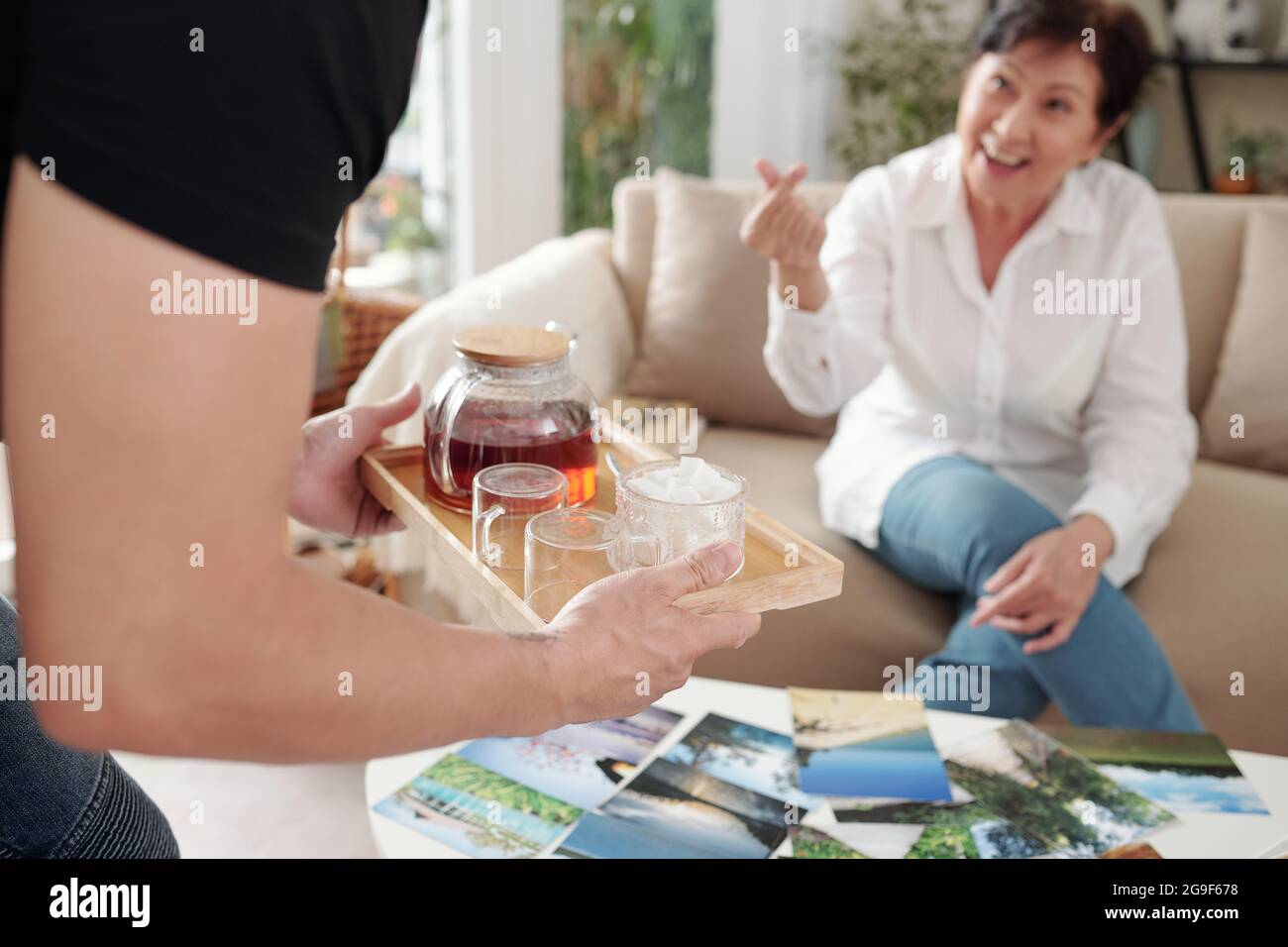 Close-up of young man holding tray with teapot and cups and treating ...