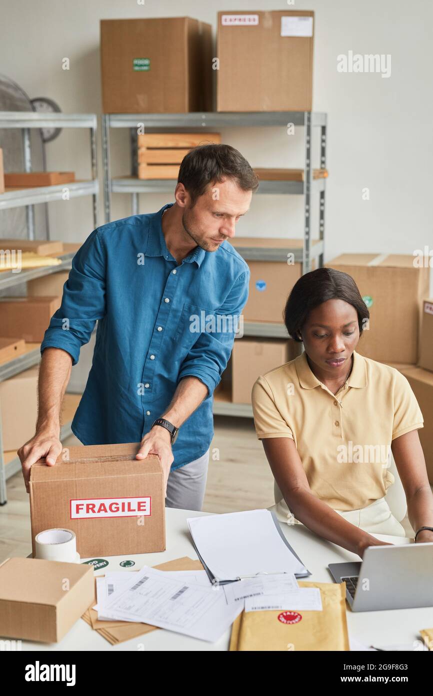 Vertical portrait of two young people using laptop in warehouse while ...