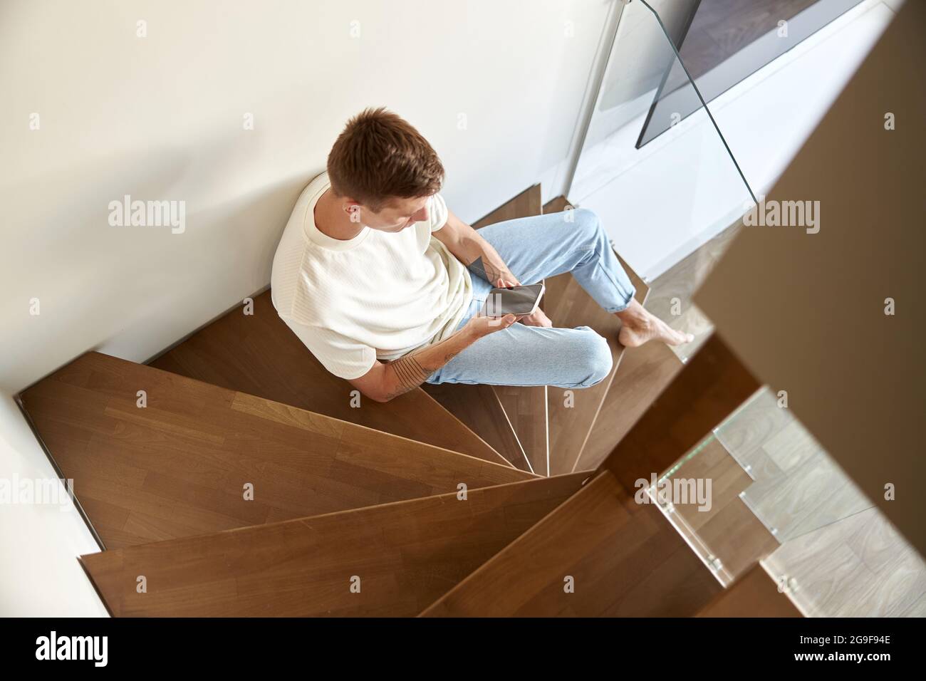 Relaxing happy caucasian man on the minimalistic stairs in modern light ...