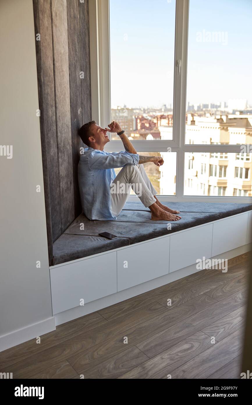 Happy adult caucasian male is sitting near panoramic window and ...