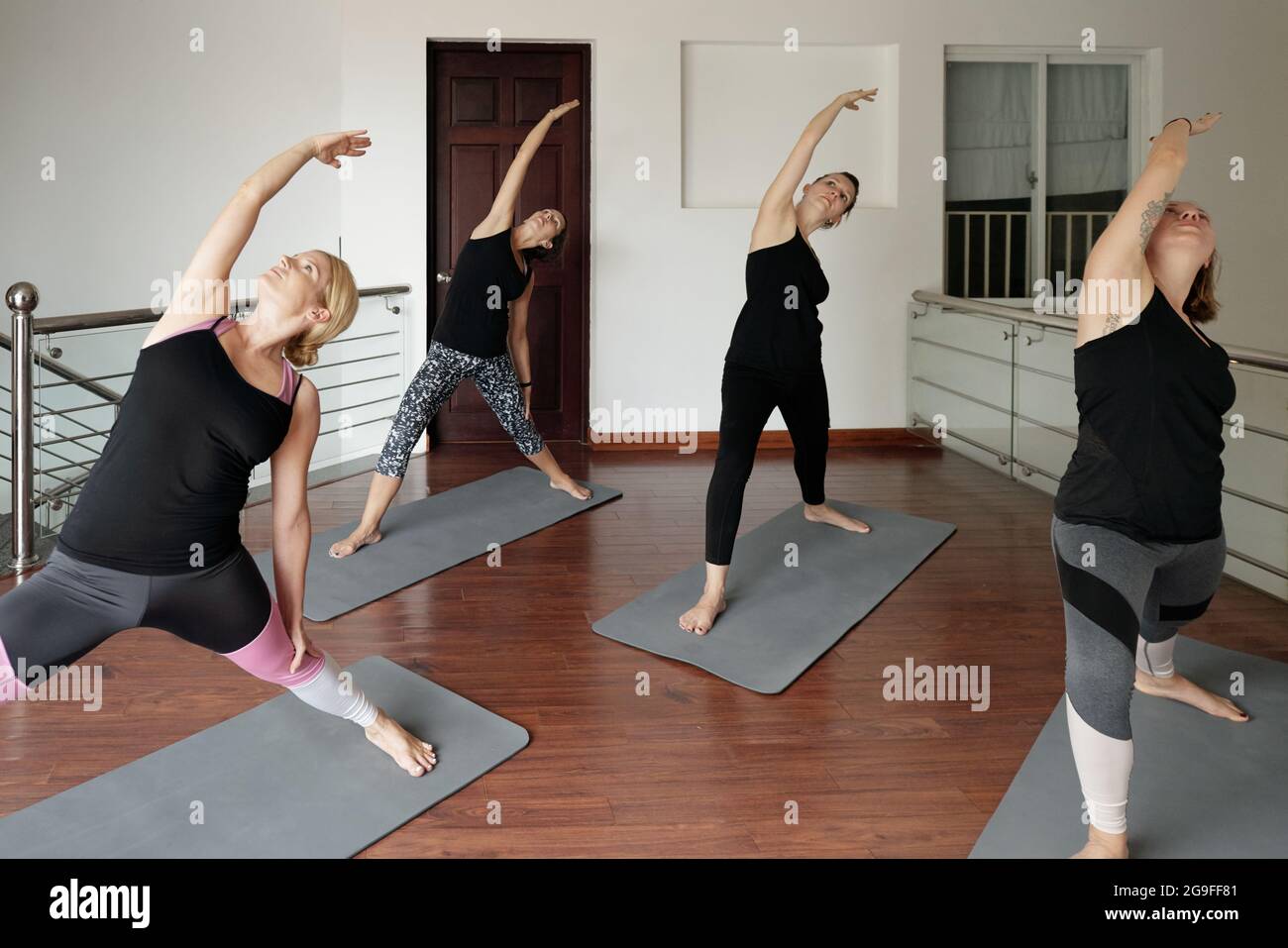 Fit young women attanding yoga class and doing reverse warrior pose ...