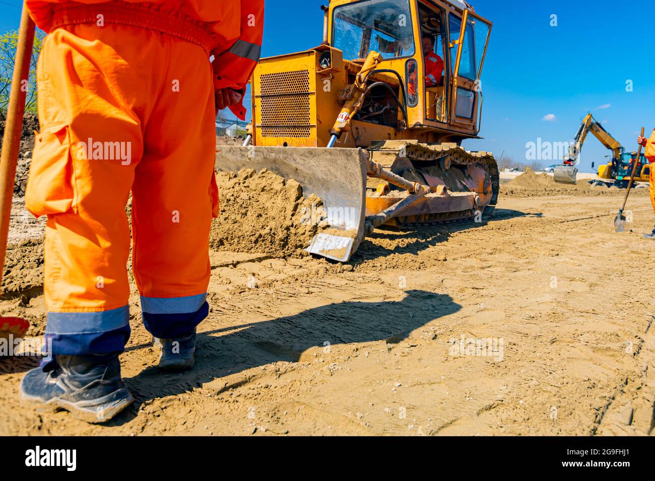 Worker stands and watches earthmover with caterpillar is moving earth ...