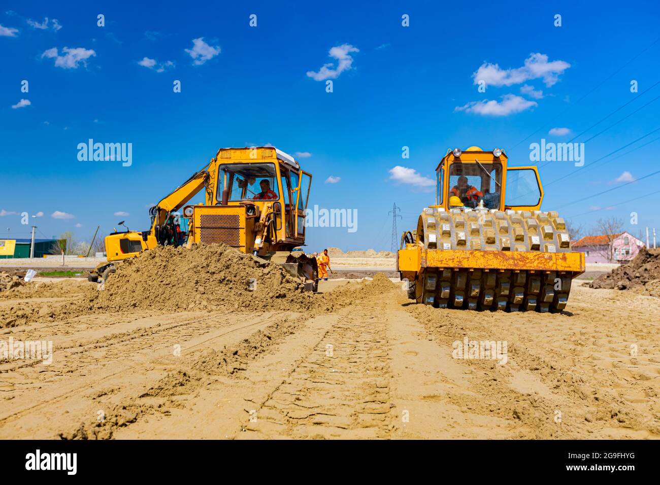 Road roller with spikes and bulldozer are compacting, leveling sand for ...