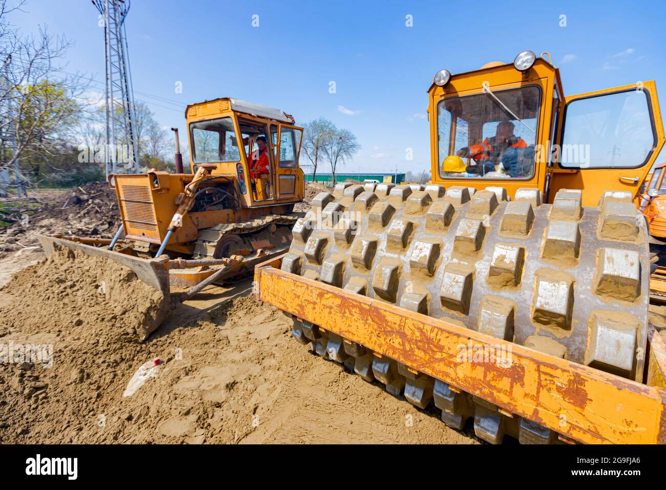 Road roller with spikes and bulldozer are compacting, leveling sand for ...