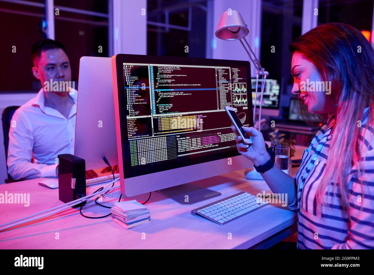 Smiling female software developer sitting at office desk and texting ...