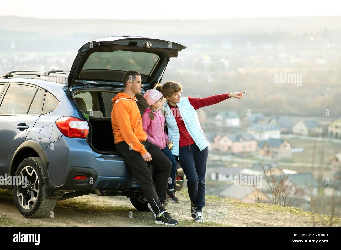 Side view of happy family standing near car with open trunk and looking ...