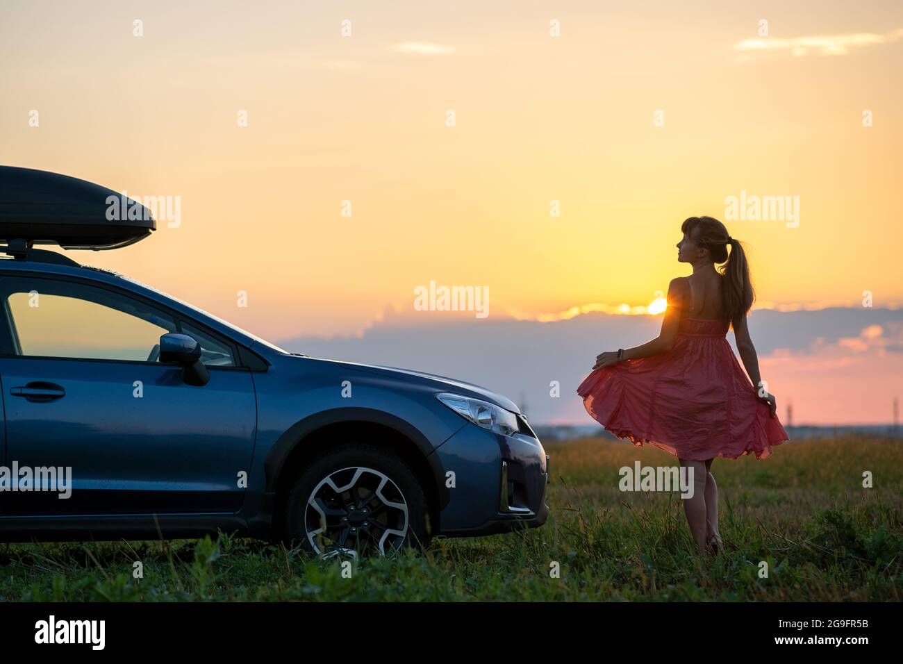 Dark silhouette of lonely woman relaxing near her car on grassy meadow ...