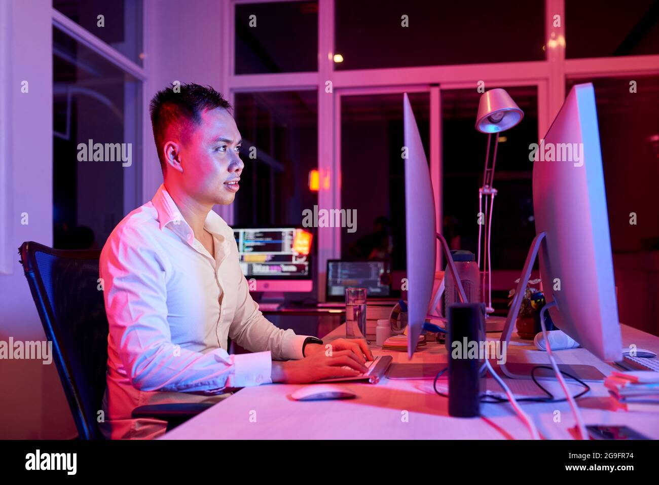 Positive software developer working on computer at office table, pink ...