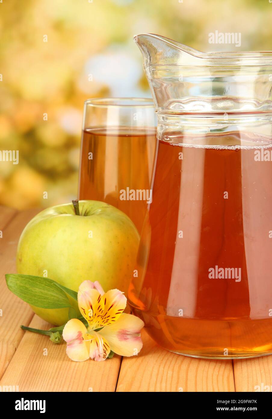 Full glass and jug of apple juice and apple on wooden table outdoor ...