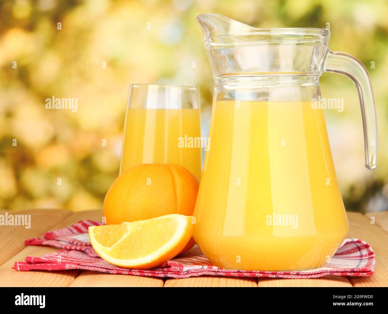 Full glass and jug of orange juice and oranges on wooden table outdoor ...