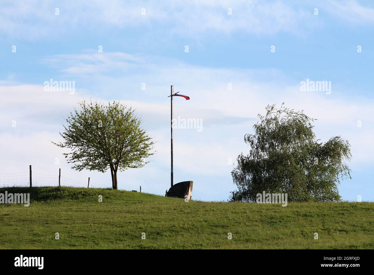 Rusted tall metal flag pole with dilapidated broken flag on top waving ...