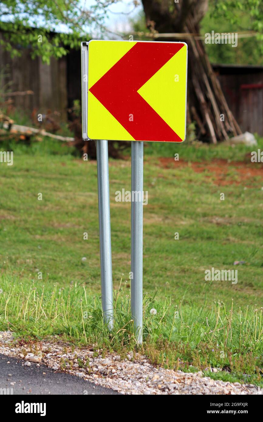 Sharp turn ahead yellow and red arrow road sign mounted on metal poles ...