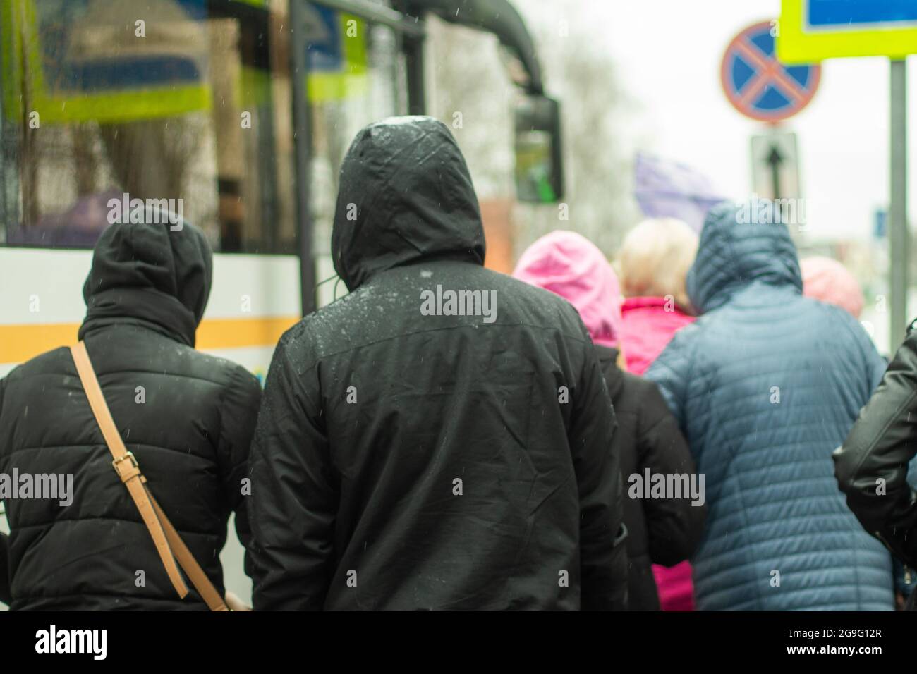 People from the back in the rain. Hooded people walk towards the bus ...