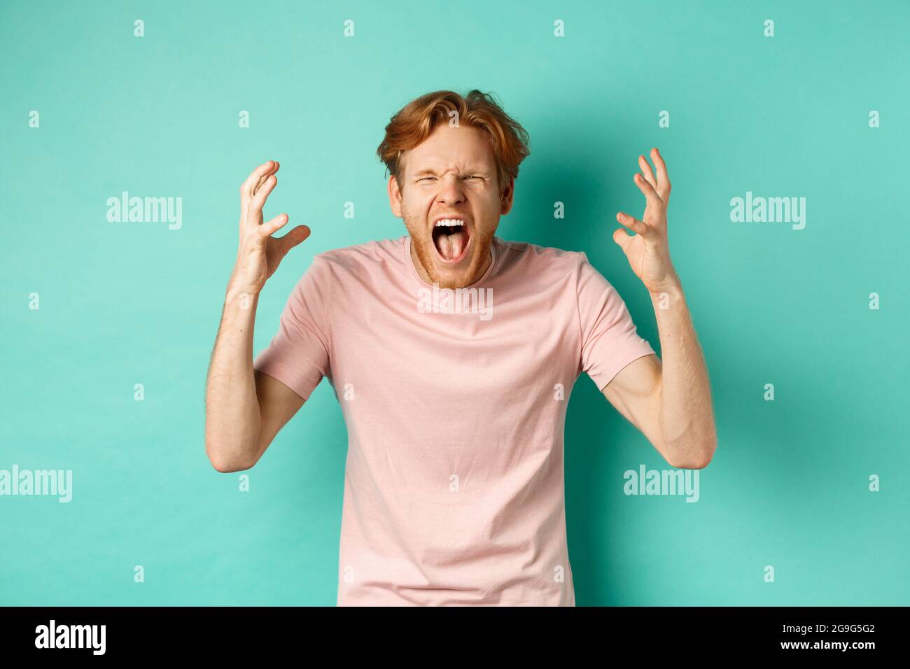Angry young redhead man screaming distressed, shaking hands and looking ...