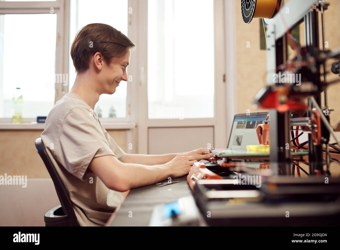 Side view of positive young man smiling and browsing pictures on laptop ...
