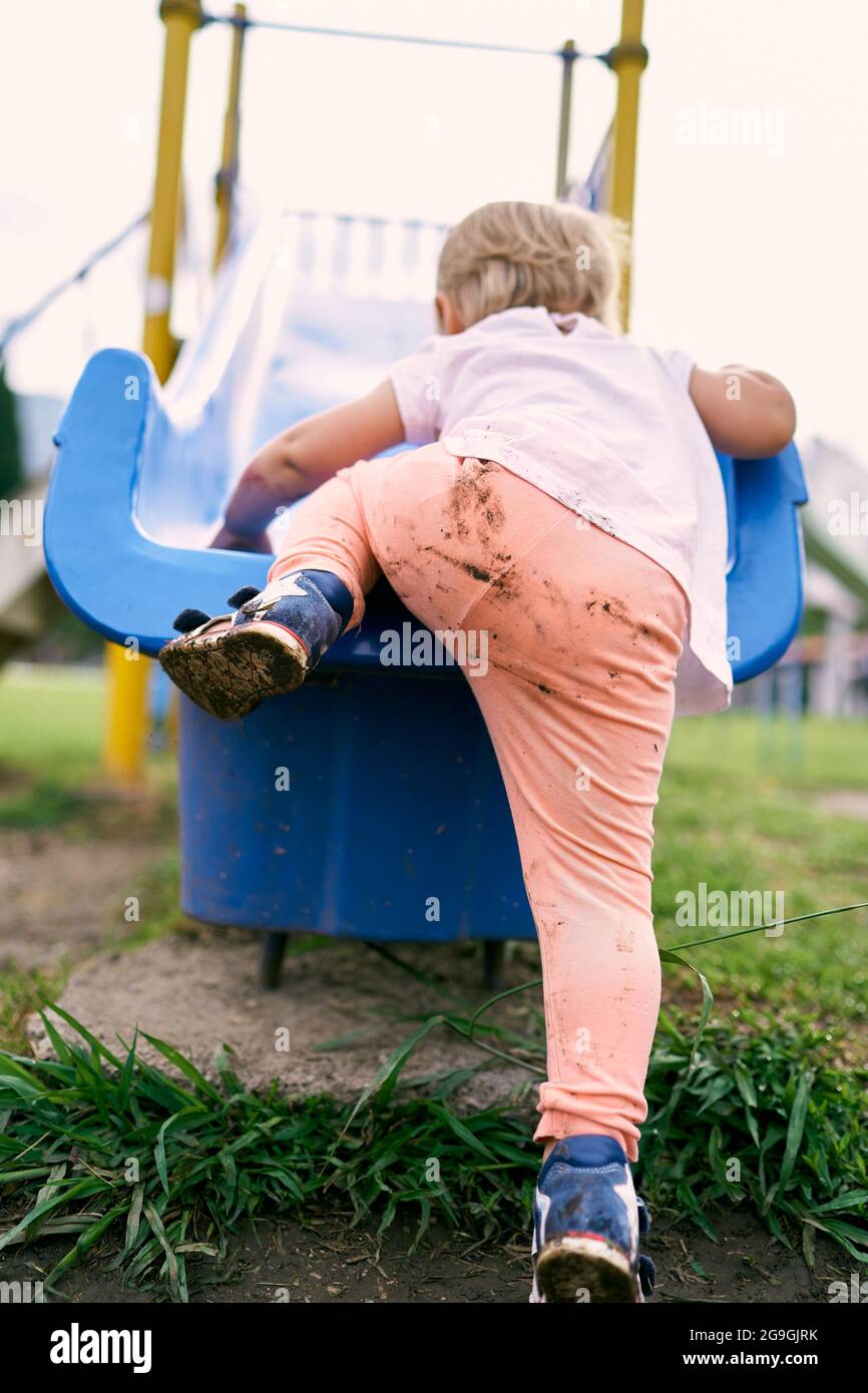 Small child in mud-stained pants climbs a slide. Close-up Stock Photo ...