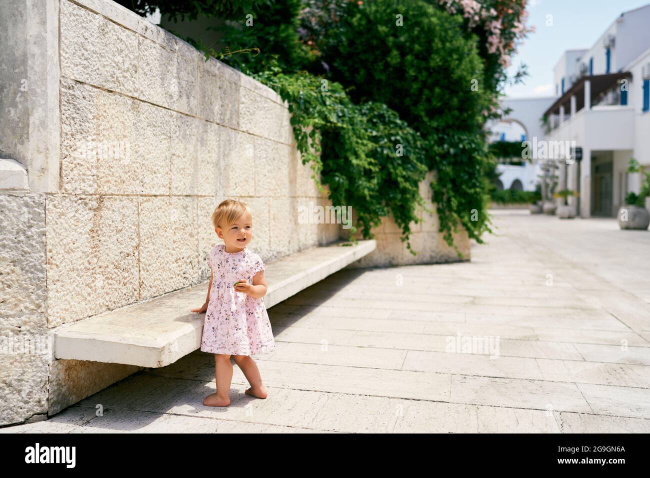 Little girl stands at a bench near a stone wall in the courtyard Stock ...