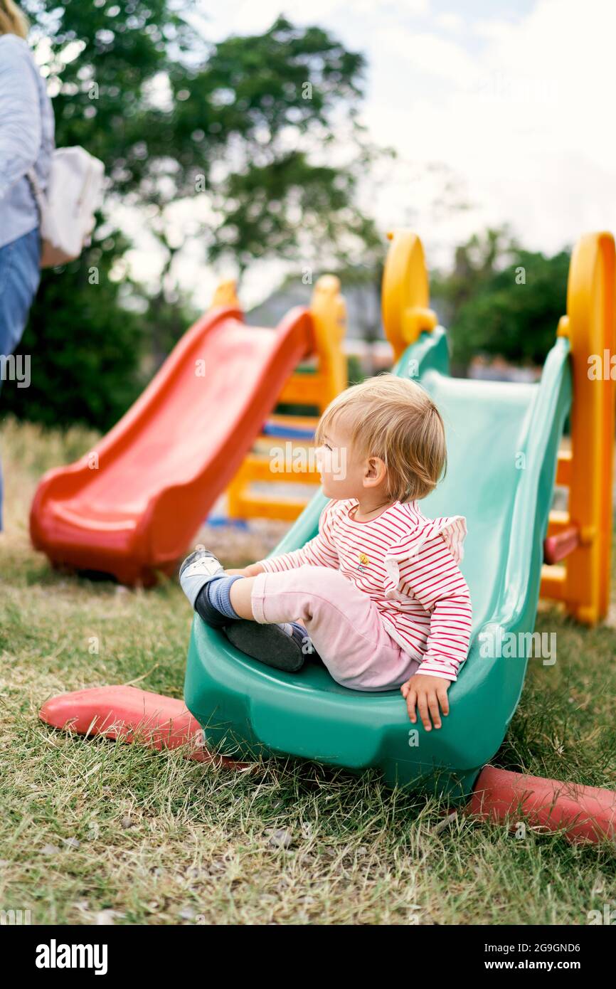 Kid sits on a children's slide on the playground. Side view Stock Photo ...