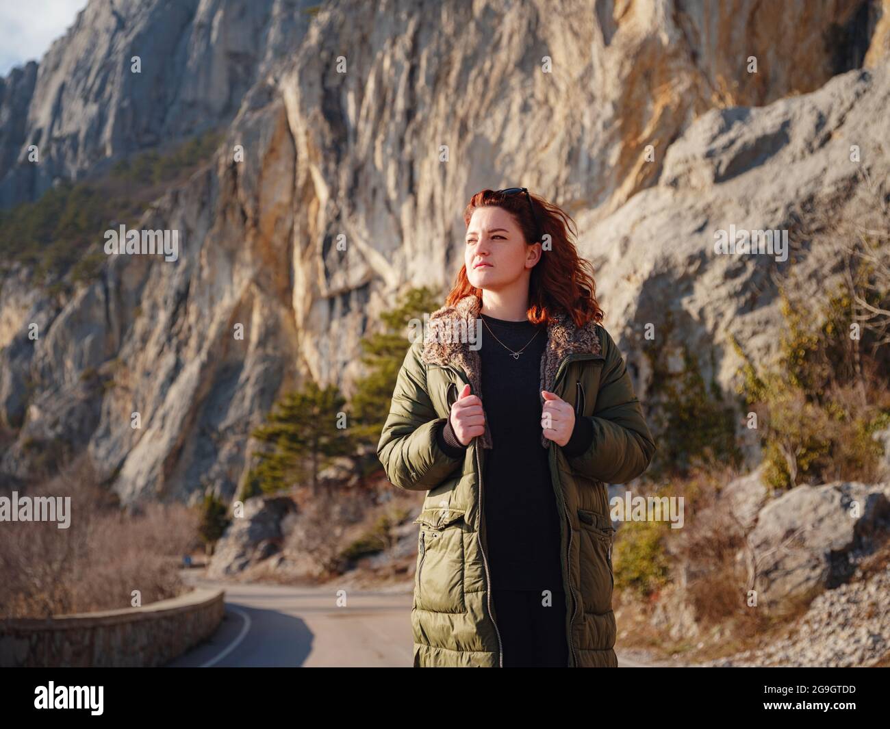 a redheaded woman walking along a mountain road in early spring. Hiker ...