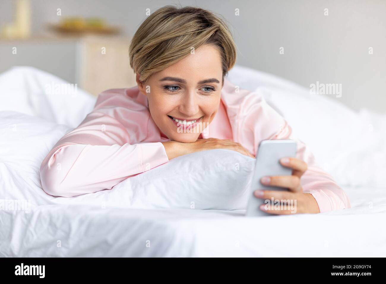 Mobile Phone User. Closeup portrait of happy woman lying in bed on ...