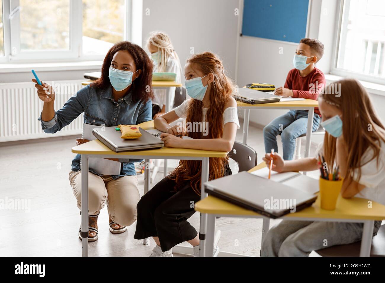 Female teacher is crouching near girl desk Stock Photo - Alamy