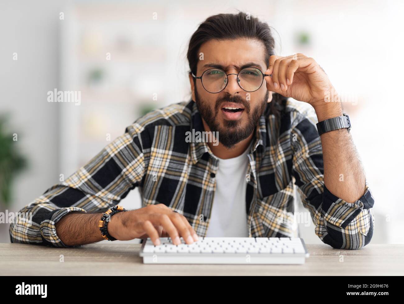 Confused middle-eastern man programmer sitting at worktable, using ...
