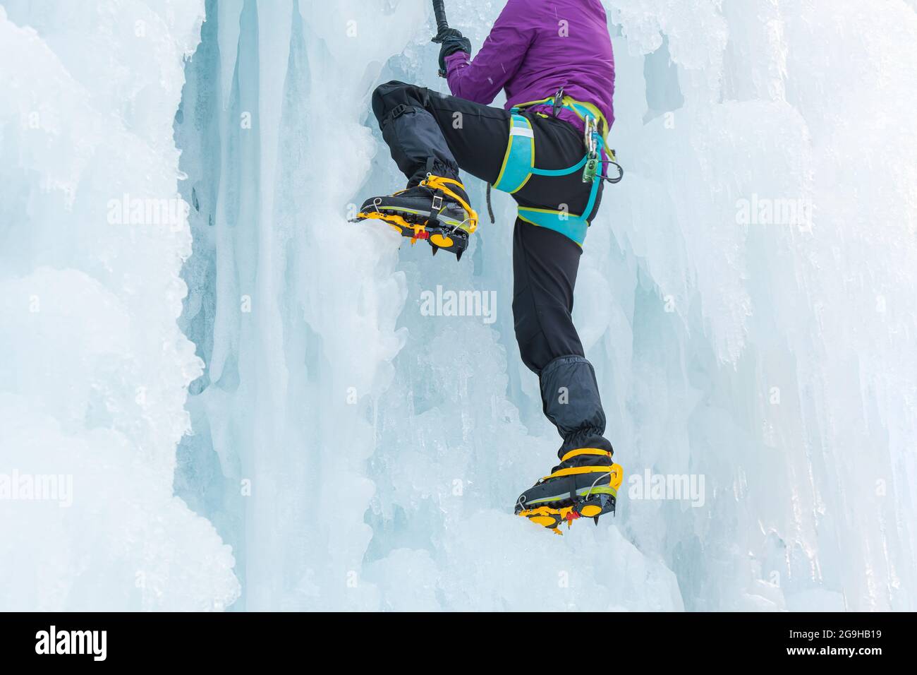Woman climbing down the side of an icy slope, hanging on a rope ...
