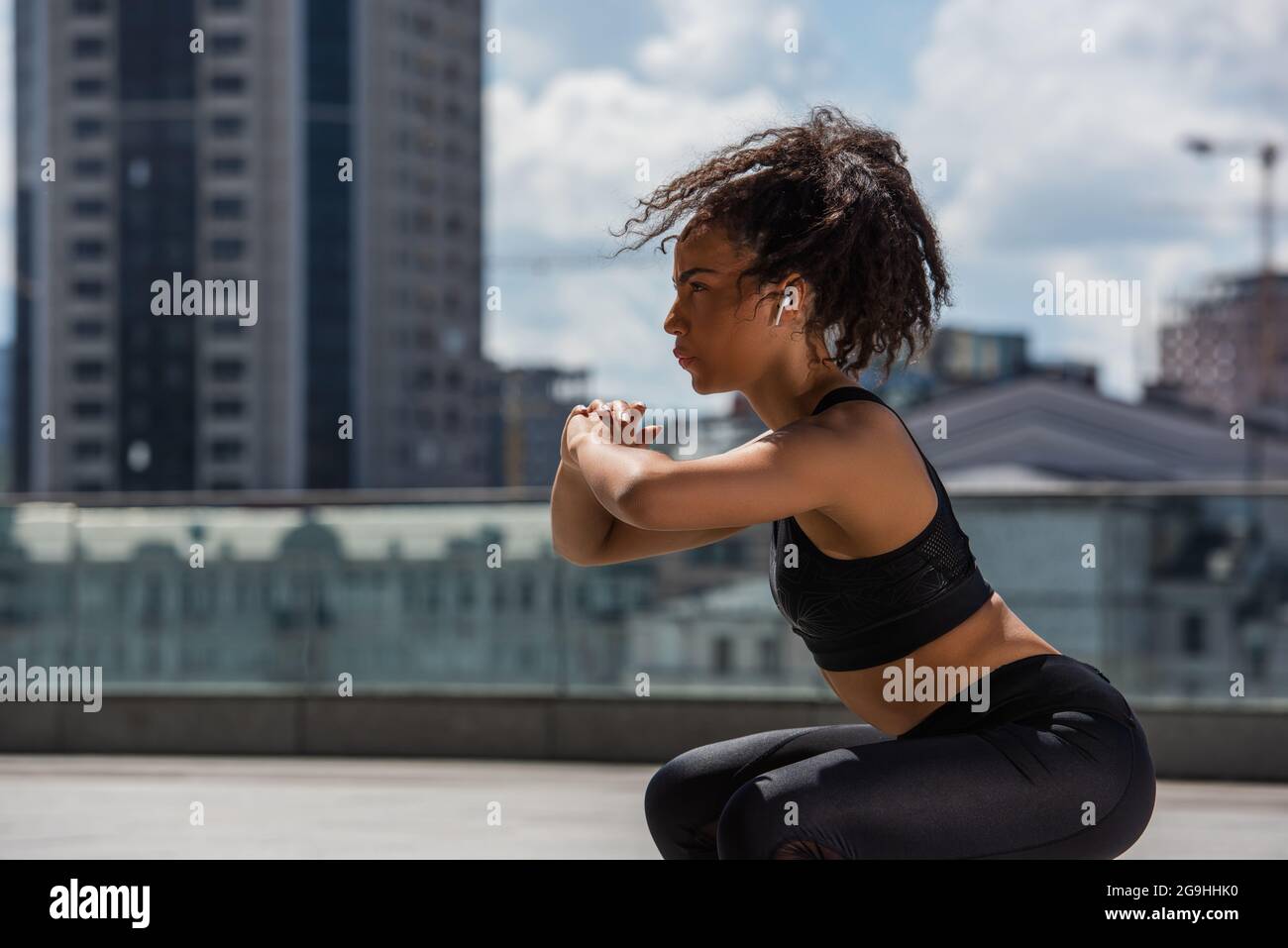 Side view of african american sportswoman in earphone doing squat on ...