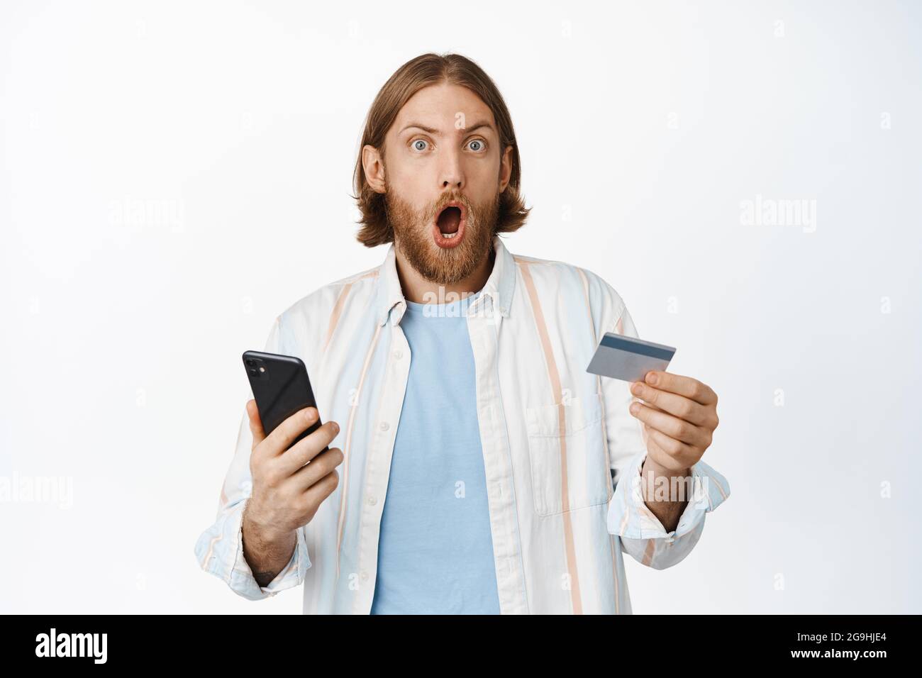 Image of surprised blond man gasp in awe, holding mobile phone and ...
