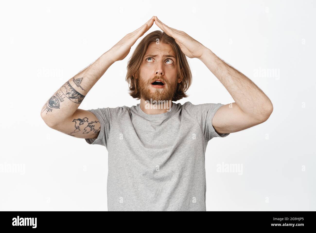 Funny blond guy squinting eyes, looking at his hands making roof ...