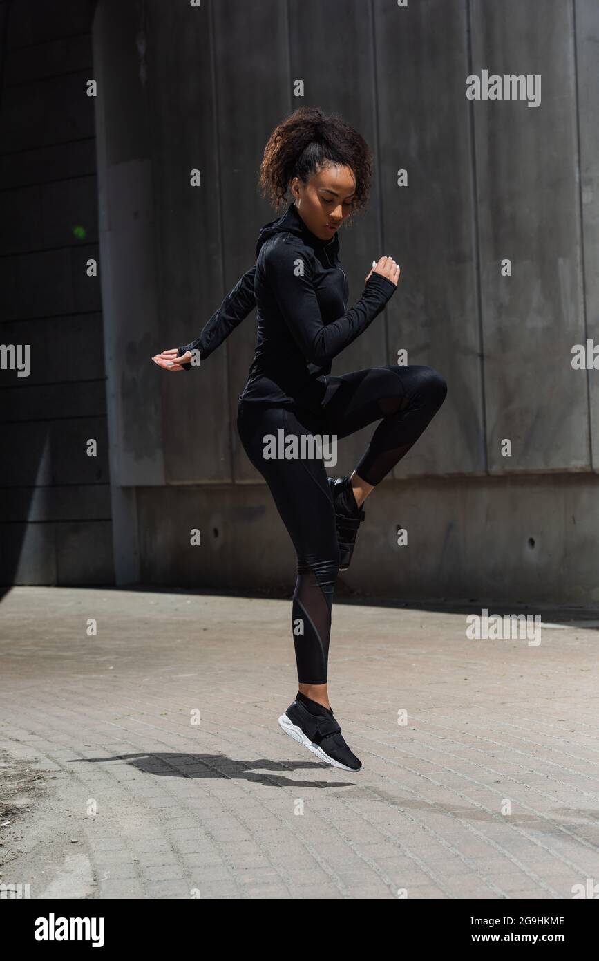 African american woman jumping while exercising on urban street Stock ...