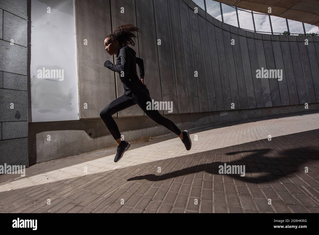 Side view of african american woman running near building with concrete ...