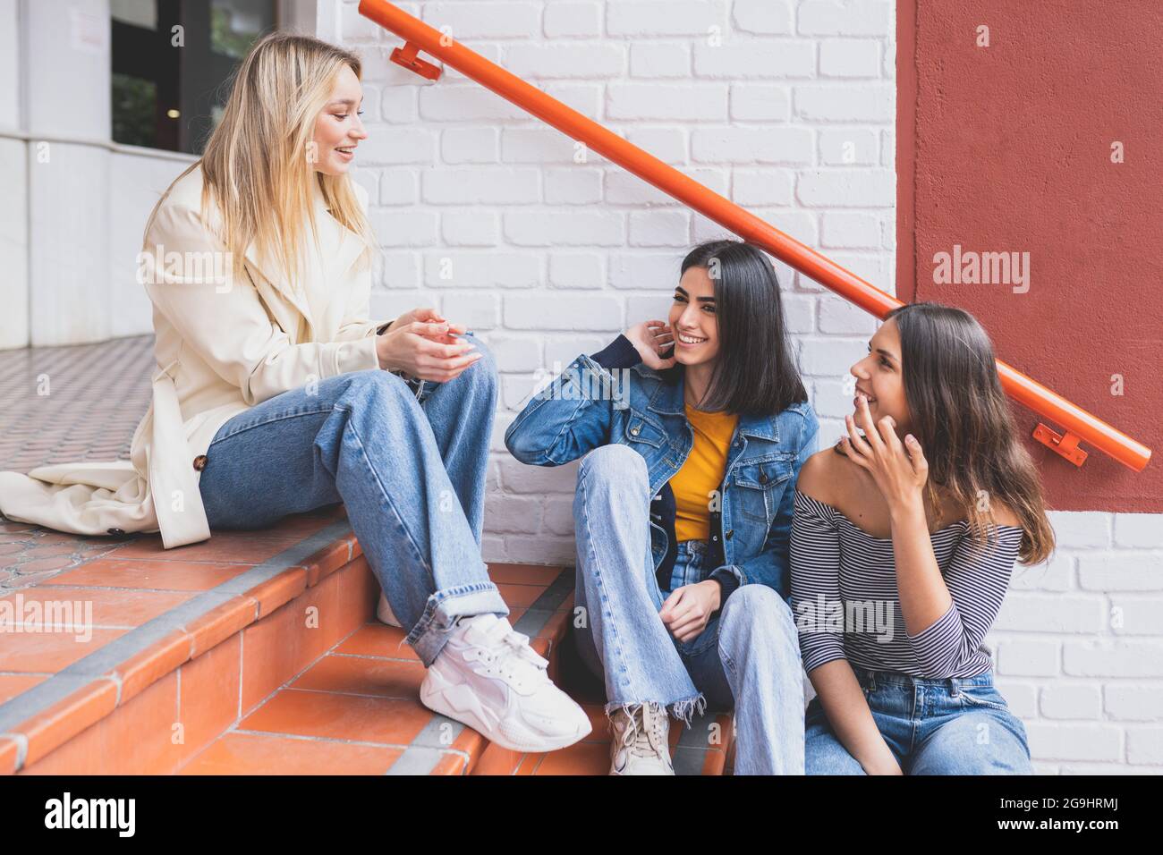 Multi-ethnic group of three friends sitting on street steps talking ...