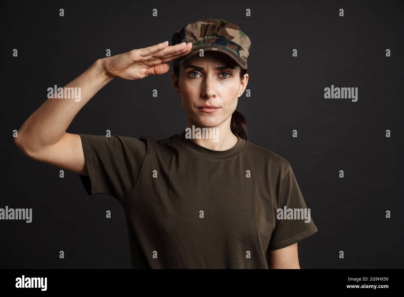 Confident beautiful soldier woman saluting and looking at camera ...