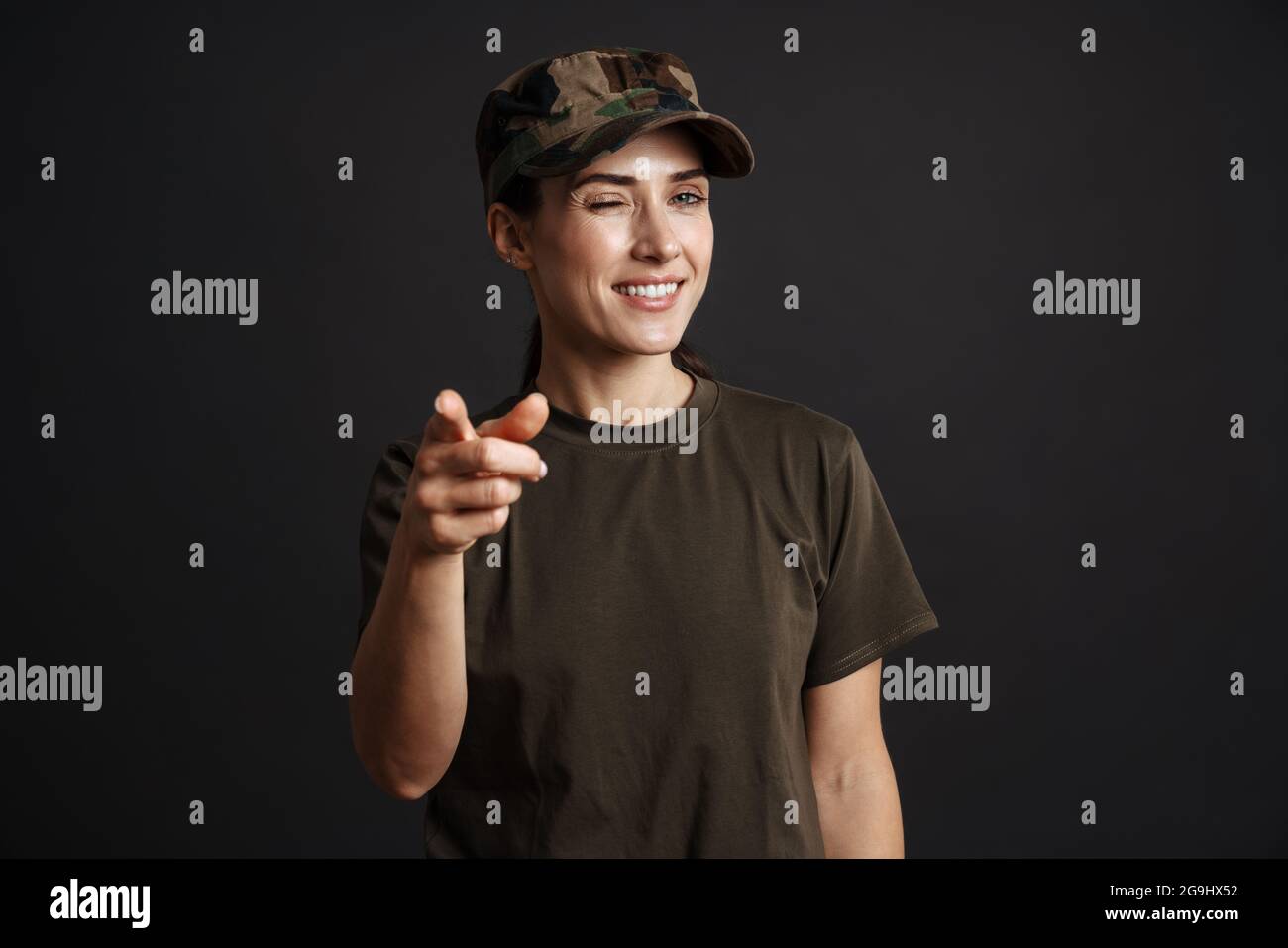 Happy soldier woman winking and pointing finger at camera isolated over ...