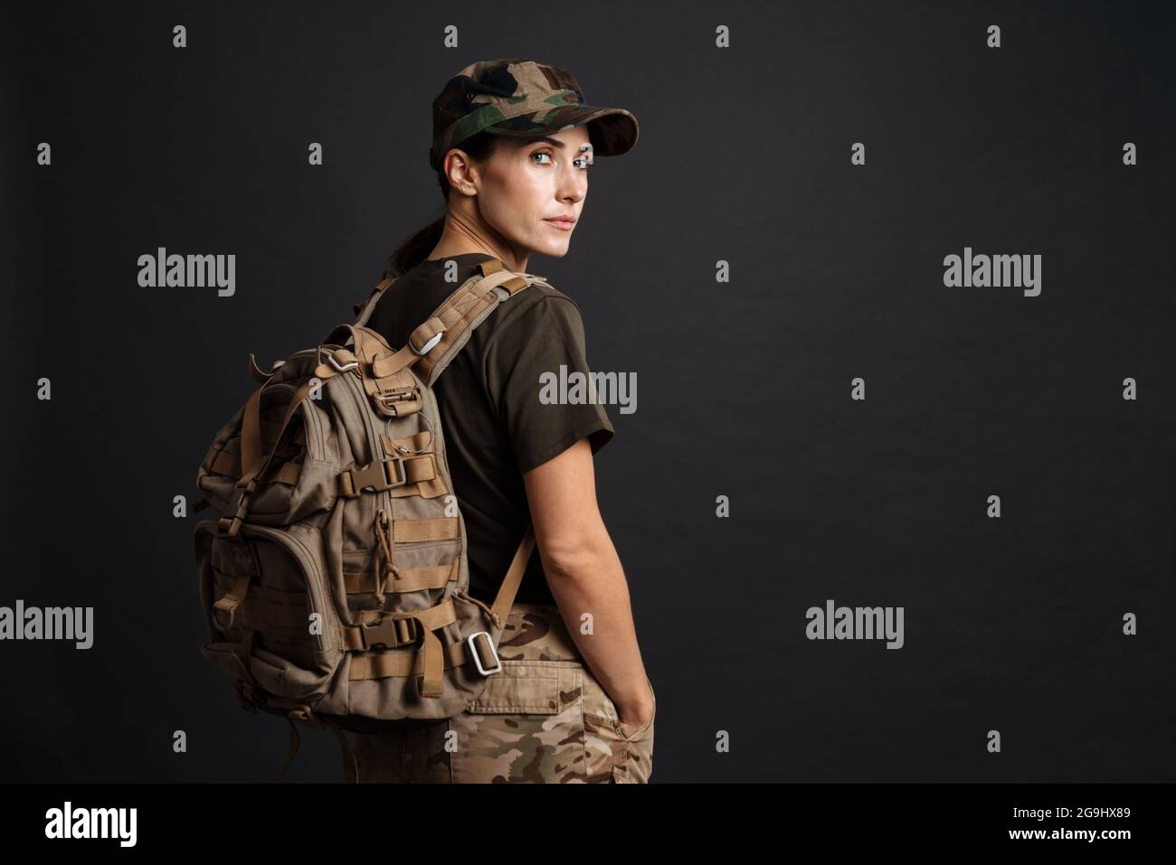 Confident soldier woman posing with backpack isolated over black wall ...